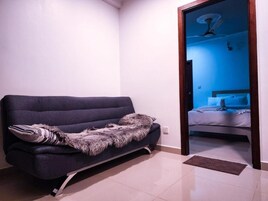 Quarto com sofá escuro, manta de pele e cama com parede e ventoinha azuis.