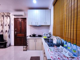 Cozinha com armários brancos, porta de madeira, fogão, micro-ondas e janela com persianas.