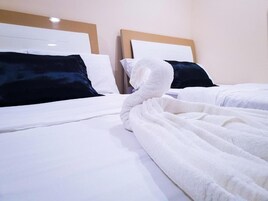 Quarto de hotel com duas camas, roupa de cama branca e almofadas escuras.