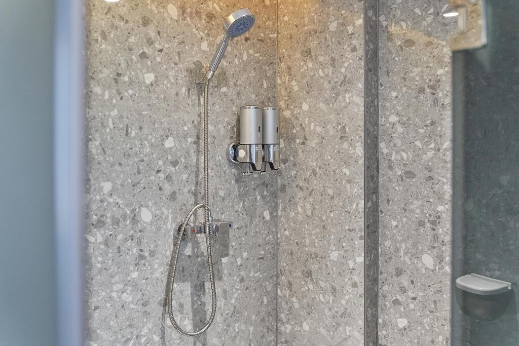 Um chuveiro com um chuveiro manual, uma torneira fixada na parede e um acessório de chuveiro manual.
