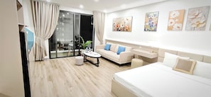 Quarto de hotel moderno com sofá, mesa de centro redonda, cama, escrivaninha e porta de vidro deslizante para a varanda.