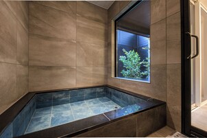 Um banheiro moderno com banheira de vidro, uma janela com vista para o verde e uma porta com puxador.