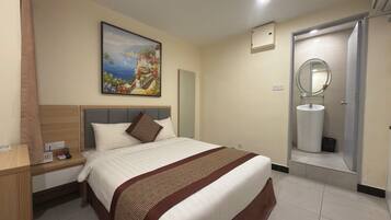 Quarto de hotel com cama, mesa de cabeceira, quadro na parede, banheiro com pia e espelho, e porta.