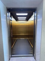 Um elevador com paredes metálicas, piso refletor e teto com iluminação fluorescente.