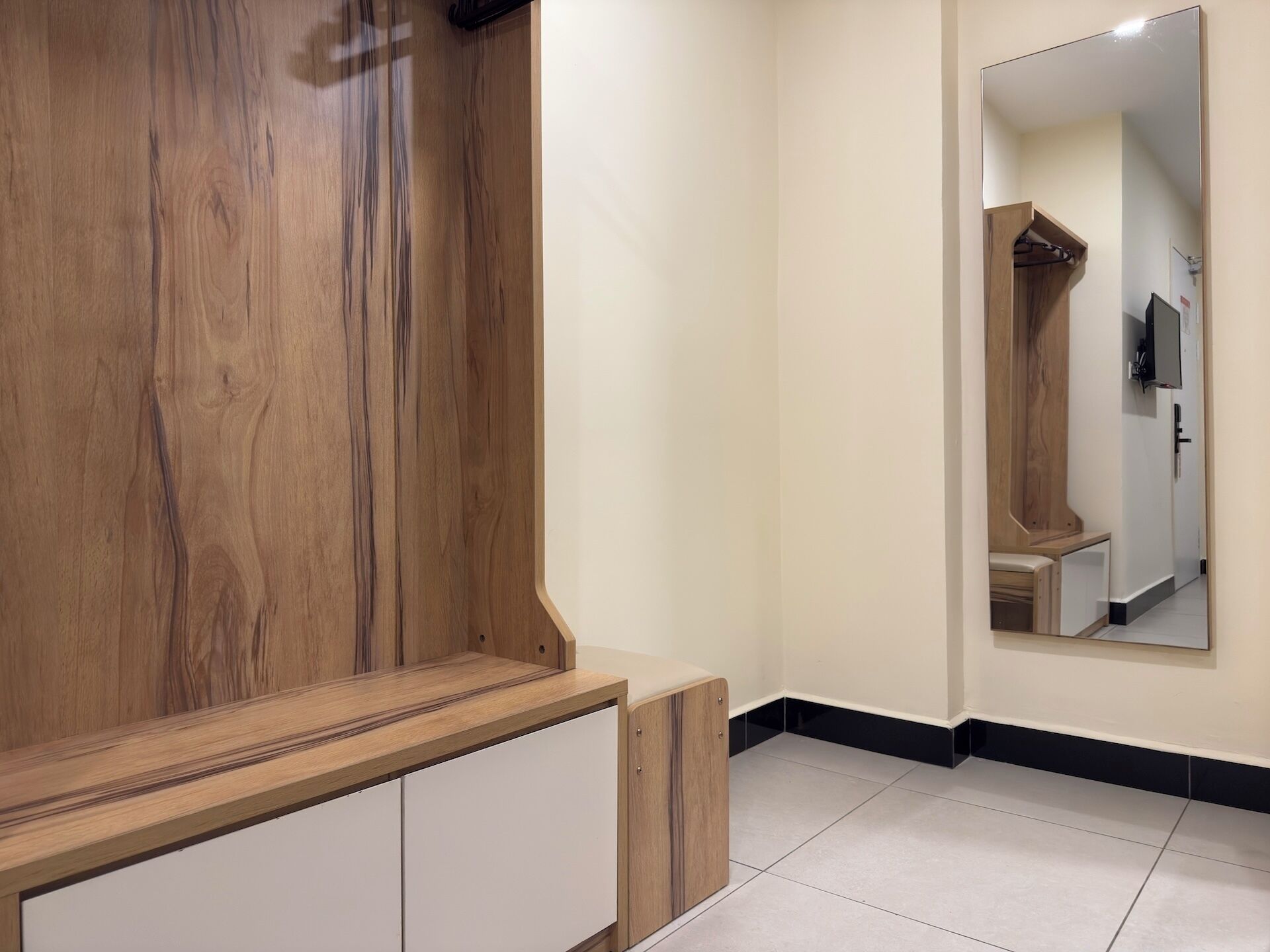 Um corredor com parede de painel de madeira, um armário branco e um espelho refletindo um guarda-roupa de madeira e uma porta.