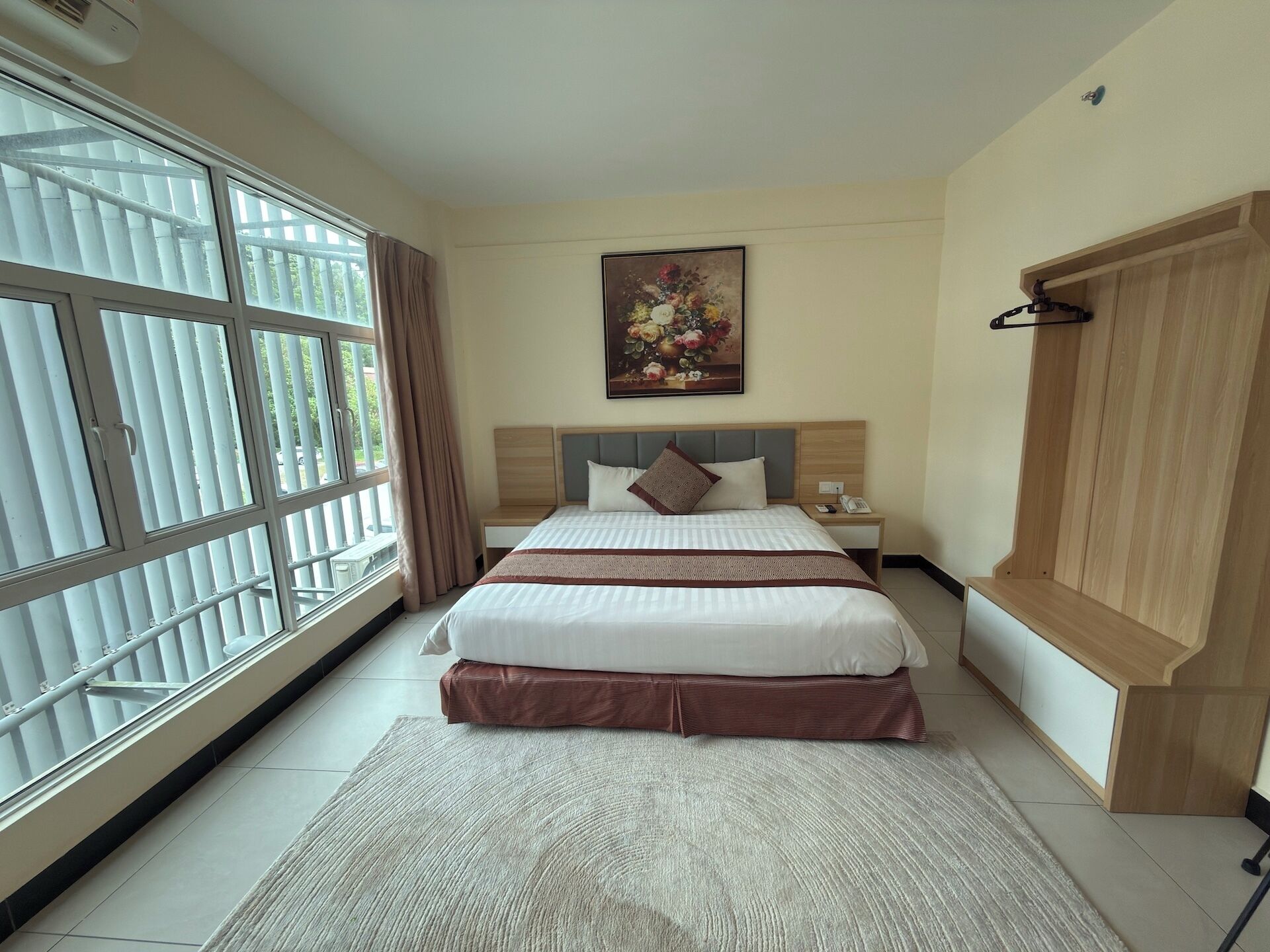 Quarto de hotel com uma janela grande, uma cama com cabeceira, uma mesa de cabeceira e um guarda-roupa.