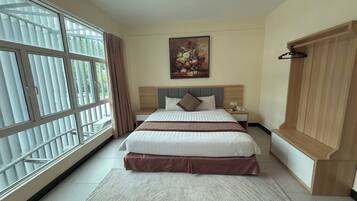 Quarto de hotel com uma janela grande, uma cama com cabeceira, uma mesa de cabeceira e um guarda-roupa.