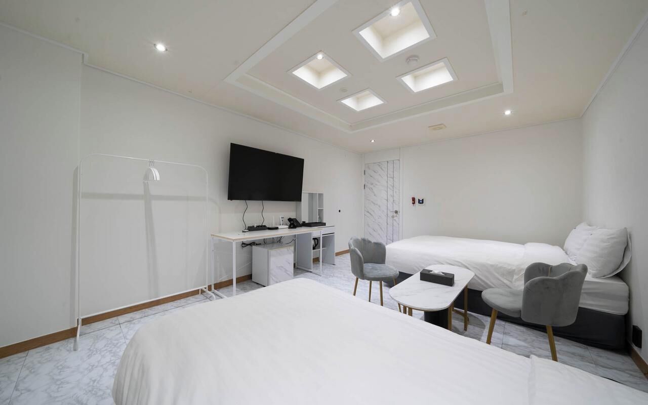 Um quarto moderno com cama, escrivaninha, cadeira, televisão e teto com claraboias.
