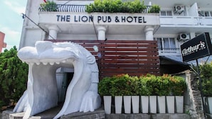 Um edifício com uma placa indicando 'The Lion Pub & Hotel' e uma grande estátua de leão branco em frente.