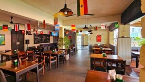 Um restaurante com várias mesas e cadeiras, bandeiras penduradas no teto e um cardápio em lousa na parede.