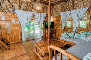 Quarto com decoração em bambu, uma cama, uma televisão e uma rede.