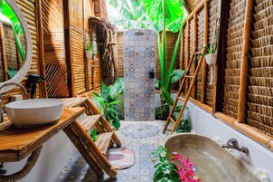 Um banheiro com uma banheira grande, um lavatório de madeira com cuba, paredes de bambu e área de chuveiro revestida com azulejos.