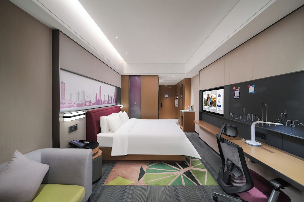 Quarto de hotel com cama, escrivaninha, cadeira e uma obra de arte com vista para a cidade.