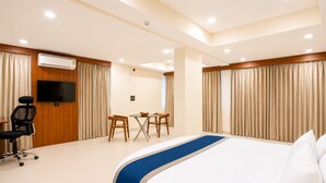 Quarto de hotel com cama, escrivaninha, duas cadeiras, televisão e ar condicionado.