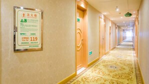 Corredor de hotel com piso coberto por carpete, sinal de segurança contra incêndio e portas de acesso aos quartos.