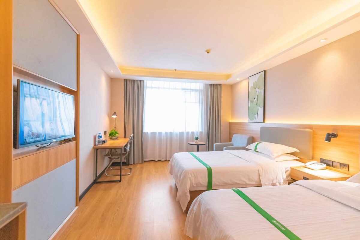 Quarto de hotel com duas camas, uma escrivaninha, televisão e janela com cortinas.