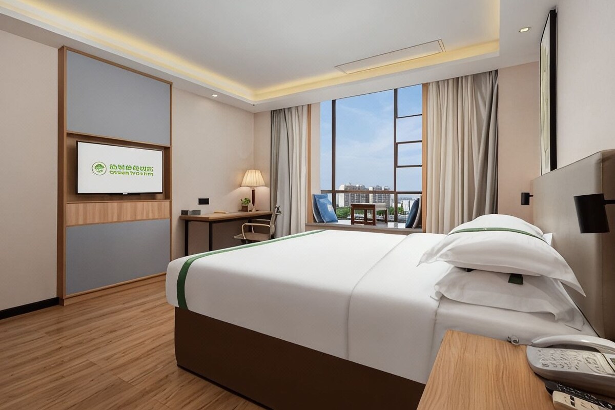 Quarto de hotel com cama, escrivaninha, cadeira e televisão na parede.