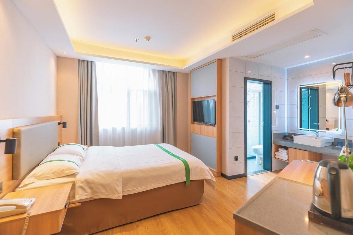 Quarto de hotel com cama, escrivaninha com telefone, televisão, banheiro com espelho e janela com cortinas.