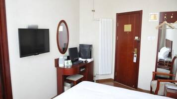 Quarto de hotel com cama, escrivaninha com computador, televisão, espelho e guarda-roupa.