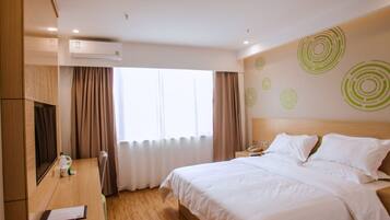 Quarto de hotel com cama, escrivaninha, cadeira, televisão e janela com cortinas.