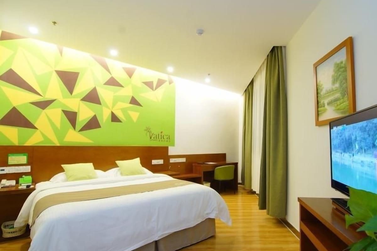 Quarto de hotel com uma cama, uma escrivaninha, uma cadeira, uma televisão e uma parede com padrões geométricos.