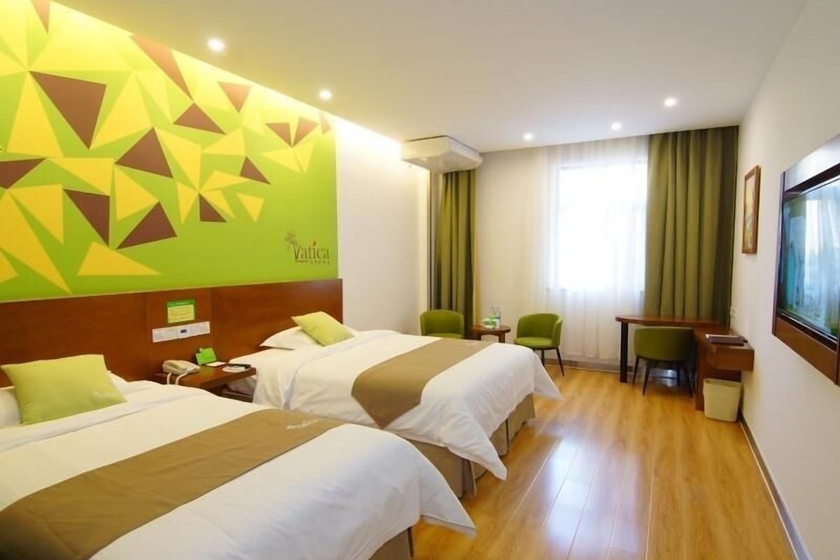 Quarto de hotel com duas camas, uma escrivaninha, uma cadeira e uma janela grande com cortinas.