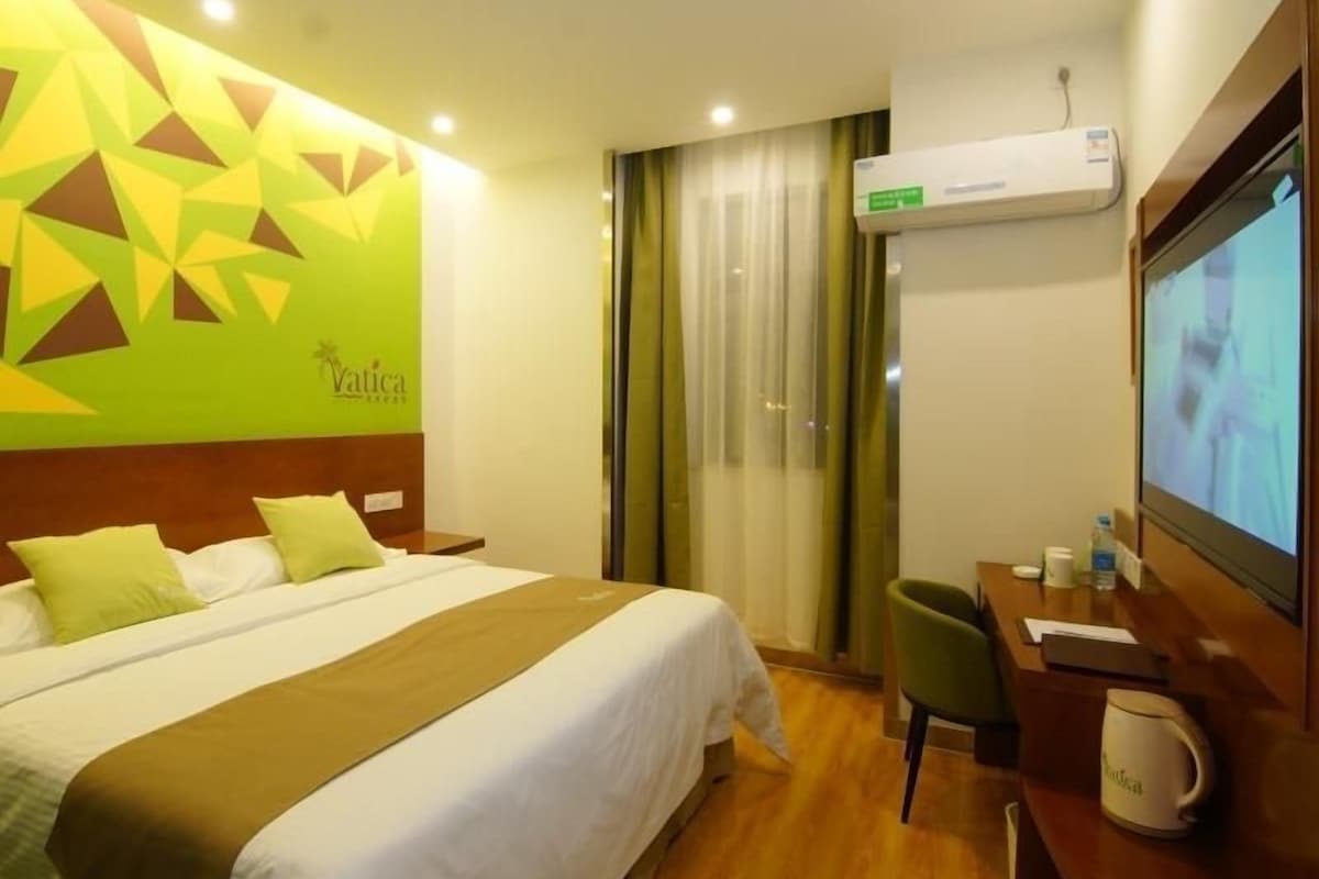Quarto de hotel com cama, escrivaninha, cadeira, ar condicionado e televisão.