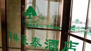 Entrada de hotel com porta de vidro, exibindo um logotipo e caracteres chineses.
