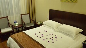 Quarto de hotel com cama, duas cadeiras, mesa de cabeceira, um quadro e janela com cortinas.