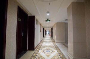 Corredor de hotel com piso estampado, portas em ambos os lados e luminária no teto.