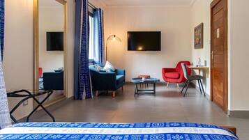 Quarto de hotel com cama, sofá, uma cadeira vermelha, mesa pequena, televisão e porta.