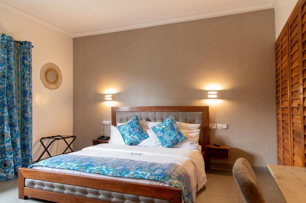 Quarto com cama, mesas de cabeceira, um banquinho e luminária na parede.