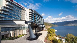 Um hotel moderno com um destaque para o letreiro 'Crowne Plaza', vista para a orla marítima e área de entrada com paisagismo.