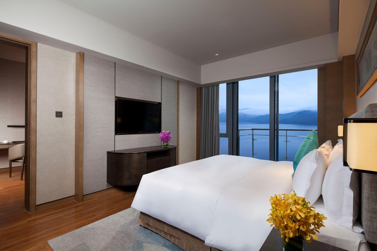 Quarto de hotel moderno com uma cama grande, televisão de tela plana, escrivaninha e vista para o mar.