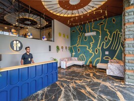 Uma área de recepção com balcão azul, piso de mármore e parede verde com arte abstrata.