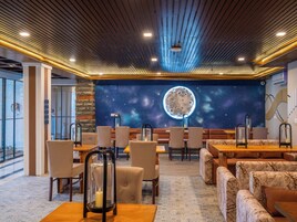 Restaurante com um mural estrelado na parede, teto de madeira e disposição de mesas.