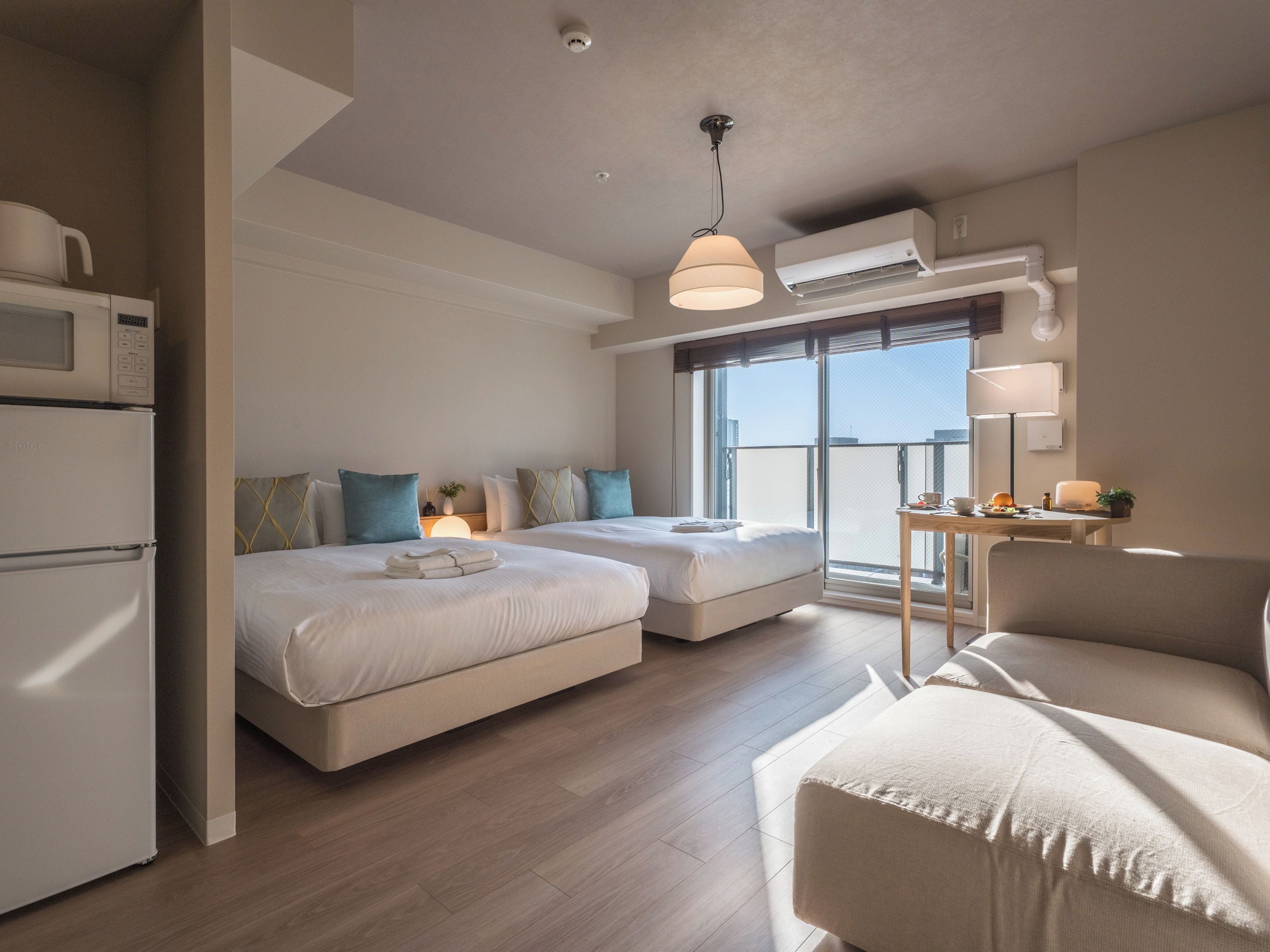 Quarto de hotel moderno com duas camas, cozinha compacta, varanda com vista e área de estar.