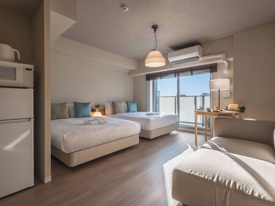 Quarto de hotel moderno com duas camas, cozinha compacta, varanda com vista e área de estar.