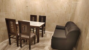 Uma sala de jantar com piso de mármore, uma mesa, quatro cadeiras e um sofá.
