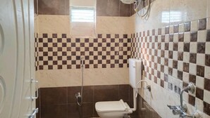 Casa de banho com chuveiro, sanita e parede com azulejos xadrez.