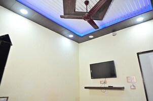 Quarto com ventilador de teto, iluminação embutida, TV fixada na parede e prateleira planejada.