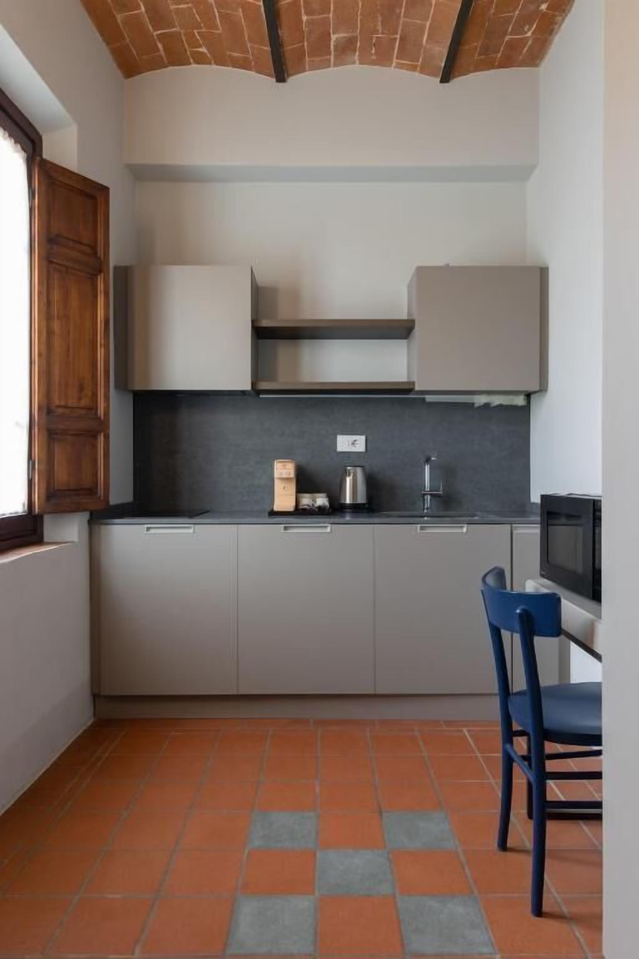 Uma cozinha compacta com armários cinza, bancada preta e piso ladrilhado.
