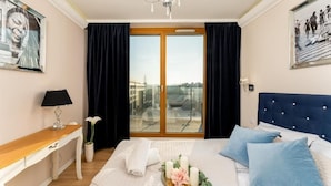 Quarto com cama, escrivaninha, cadeira, abajur, planta em vaso e vista através de uma porta de vidro.