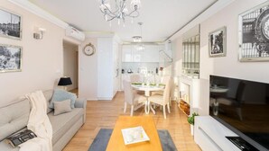 Uma sala de estar moderna com um sofá, mesa de centro e televisão. Há também uma área de refeições com mesa e cadeiras.