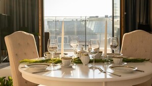 Mesa de jantar redonda posta para quatro pessoas, com louça branca, velas e plantas.