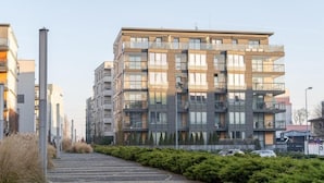 Um edifício residencial moderno, de vários andares, com varandas, um caminho pavimentado e carros estacionados.