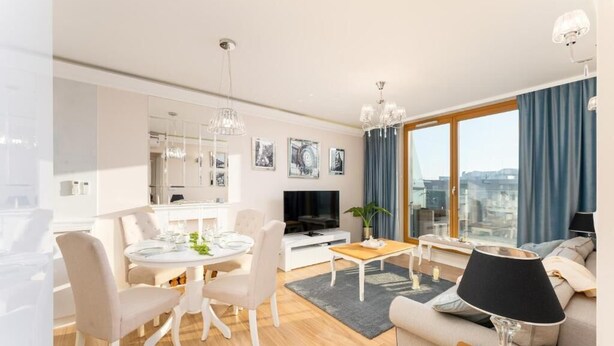 Uma sala de estar moderna com área de jantar, televisão e janelas grandes com cortinas.