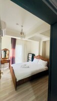 Quarto de hotel com cama de madeira, escrivaninha, cadeira e janela com cortinas.