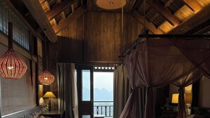 Quarto com teto de madeira, cama com dossel, sofá e mesa com abajur.