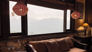 Um quarto acolhedor com sofá, uma mesa com copos e garrafa, e vista para montanhas através de grandes janelas.